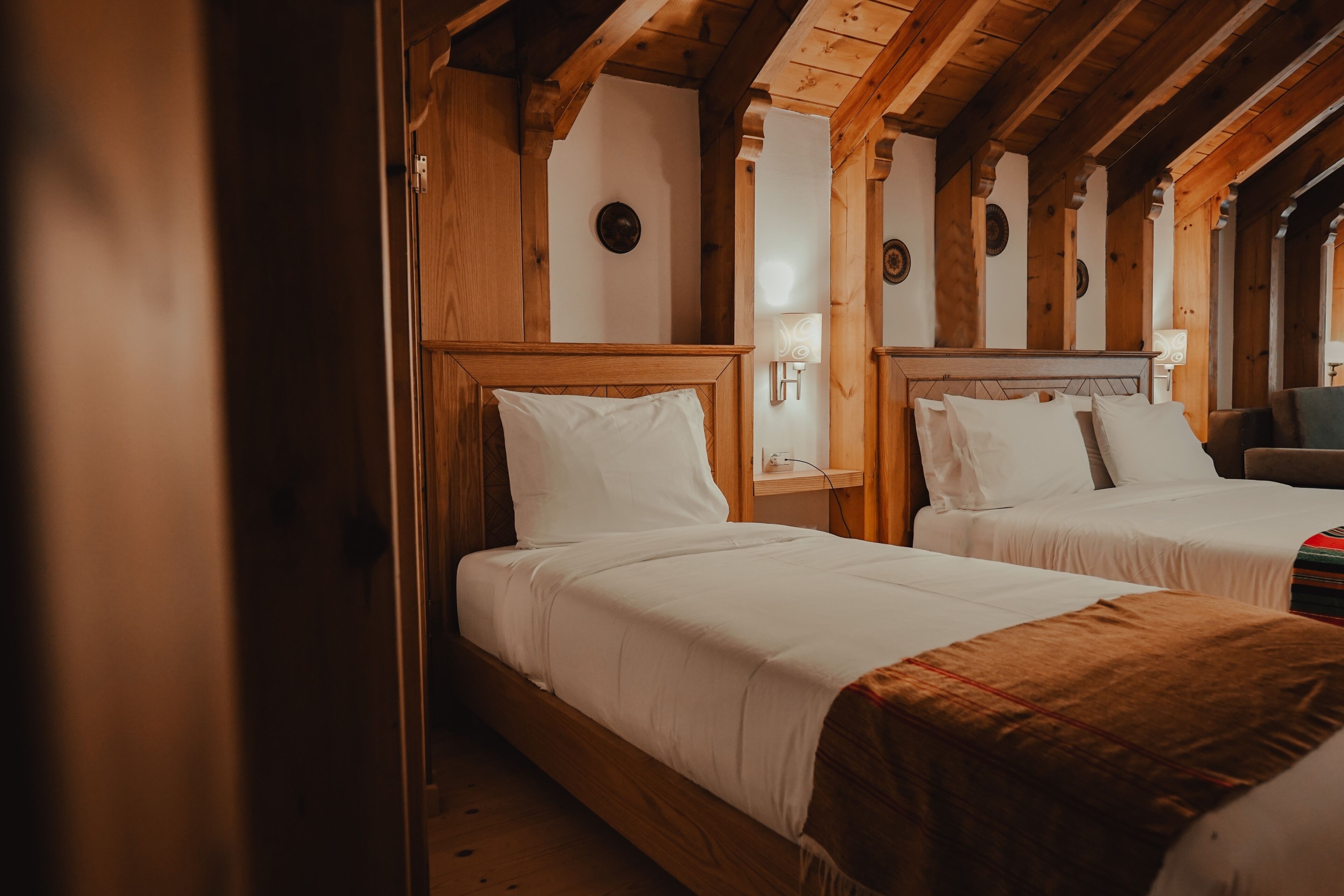Quarto de madeira com duas camas, cada uma com roupa de cama branca e cabeceira de madeira.