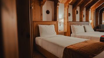 Quarto de madeira com duas camas, cada uma com roupa de cama branca e cabeceira de madeira.