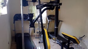 Ginásio em casa com esteira, banco de musculação e equipamentos de exercício.