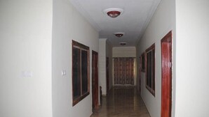 Um corredor estreito com portas de madeira em ambos os lados, chão de azulejos e teto com iluminação embutida.