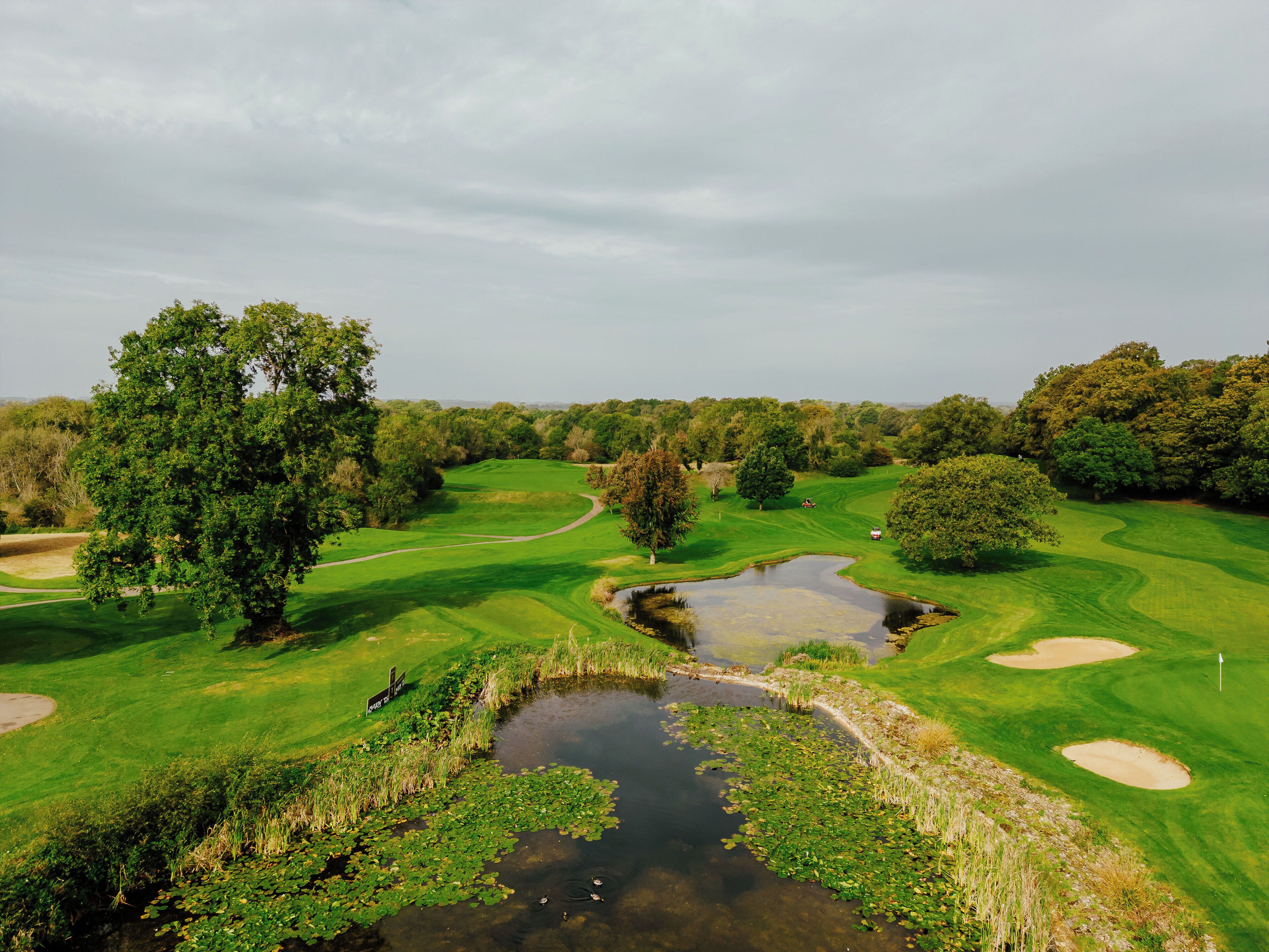 Um campo de golfe com lago, árvores e céu claro.