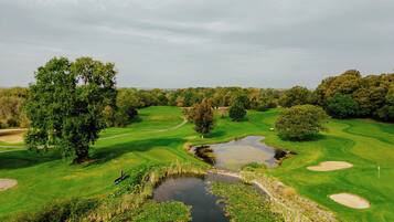 Um campo de golfe com lago, árvores e céu claro.