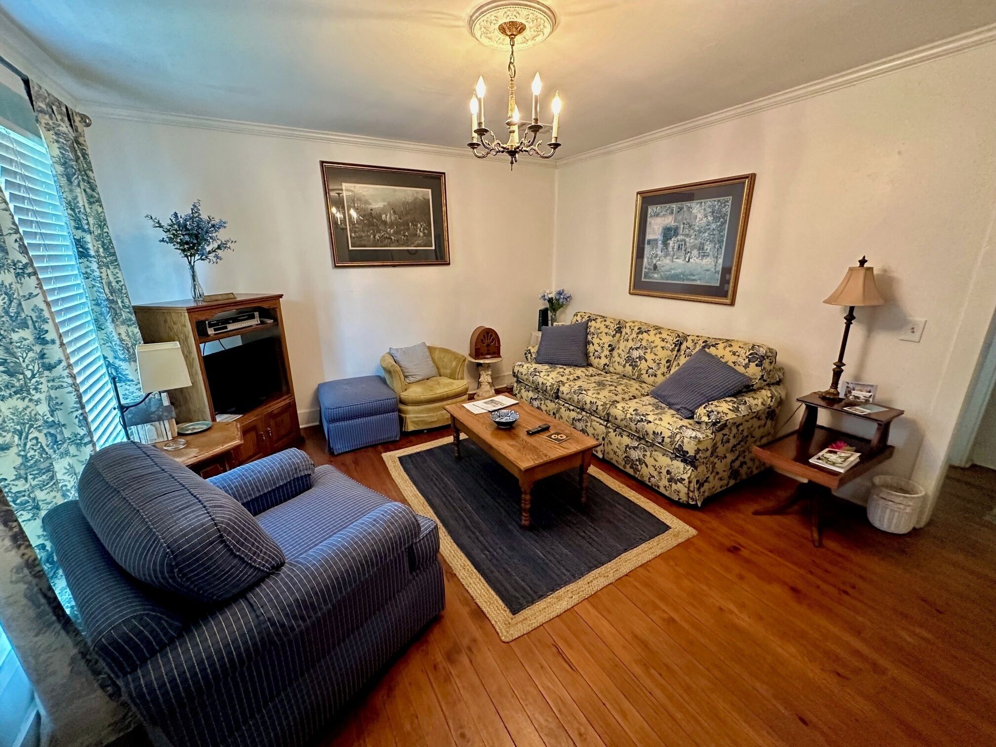 Uma sala de estar com sofá, poltrona, banqueta, mesa de centro e televisão.