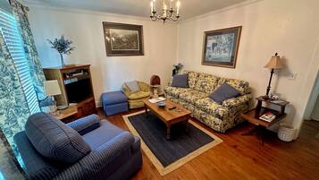Uma sala de estar com sofá, poltrona, banqueta, mesa de centro e televisão.