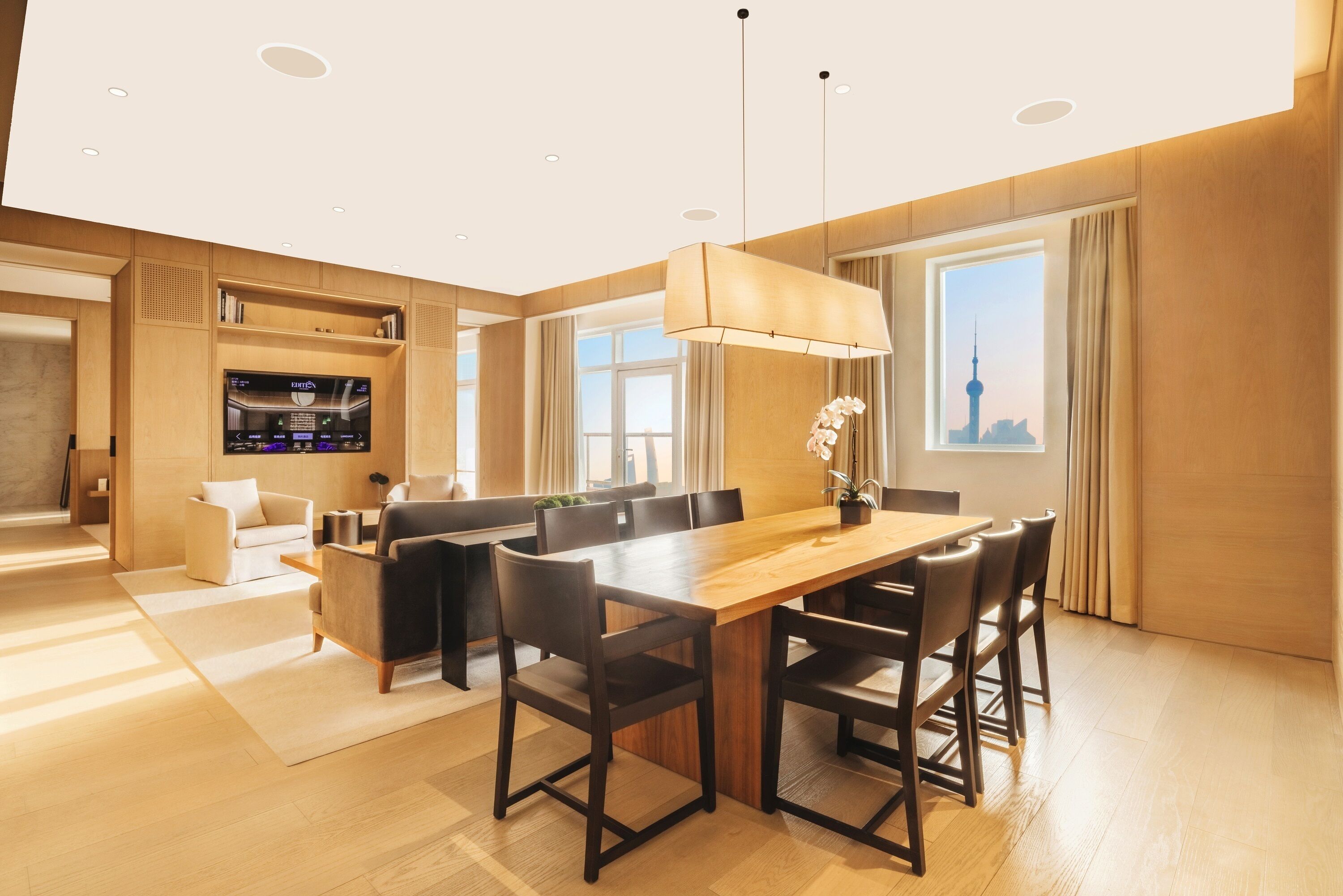 Quarto de hotel moderno com uma grande mesa de jantar, assentos confortáveis, televisão de tela plana e vista para o horizonte da cidade.