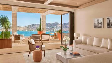Uma sala de estar moderna com uma grande janela com vista para a paisagem costeira. Há um sofá, uma mesa de centro e um espaço de jantar com cadeiras e uma mesa.