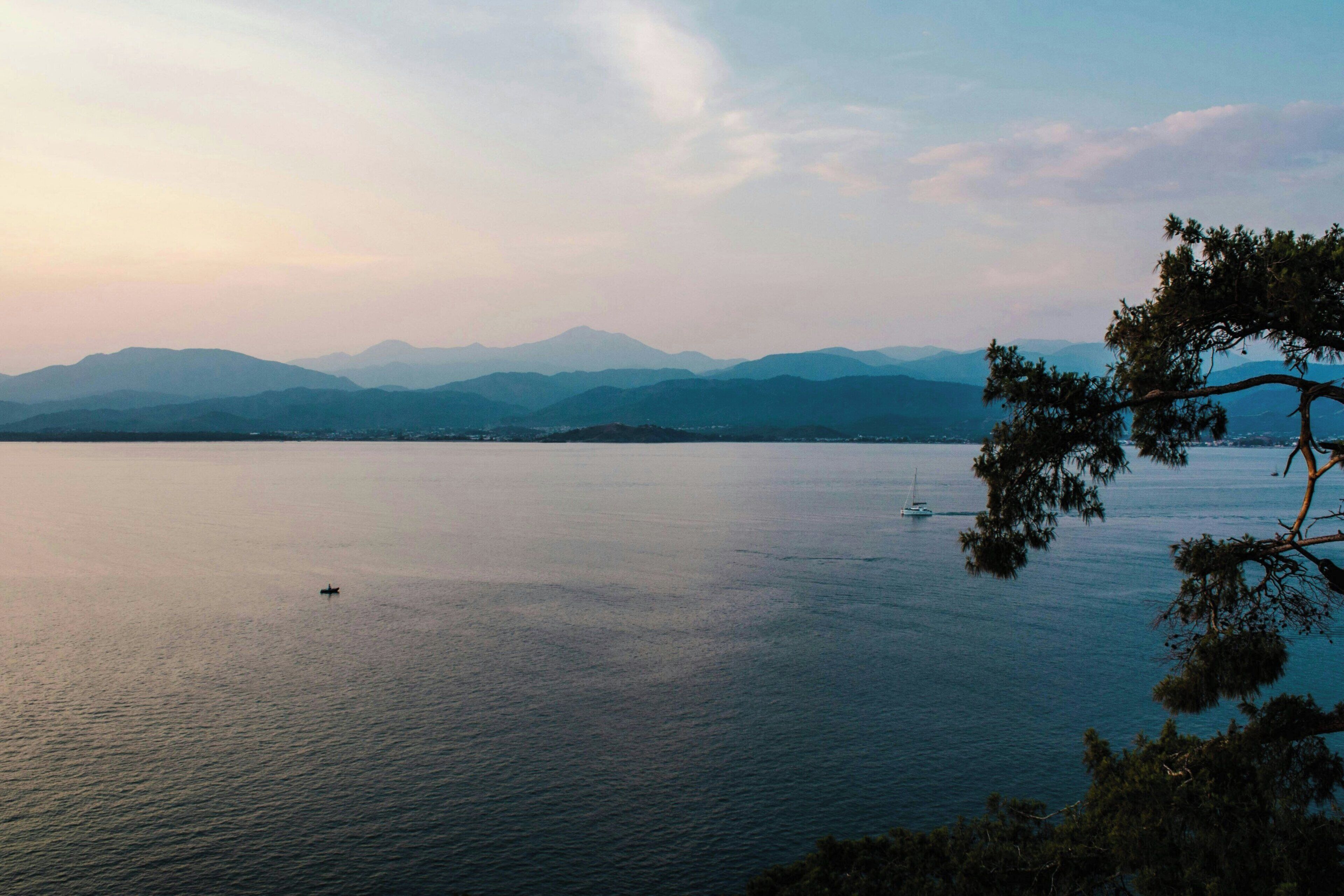 Um lago calmo com montanhas ao fundo e um galho de árvore em primeiro plano.