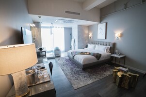 Quarto de hotel moderno com uma cama grande, mesas de cabeceira, uma escrivaninha e uma luminária.