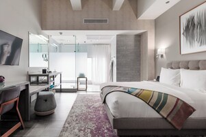 Quarto de hotel moderno com cama, escrivaninha, cadeira e um espelho grande.