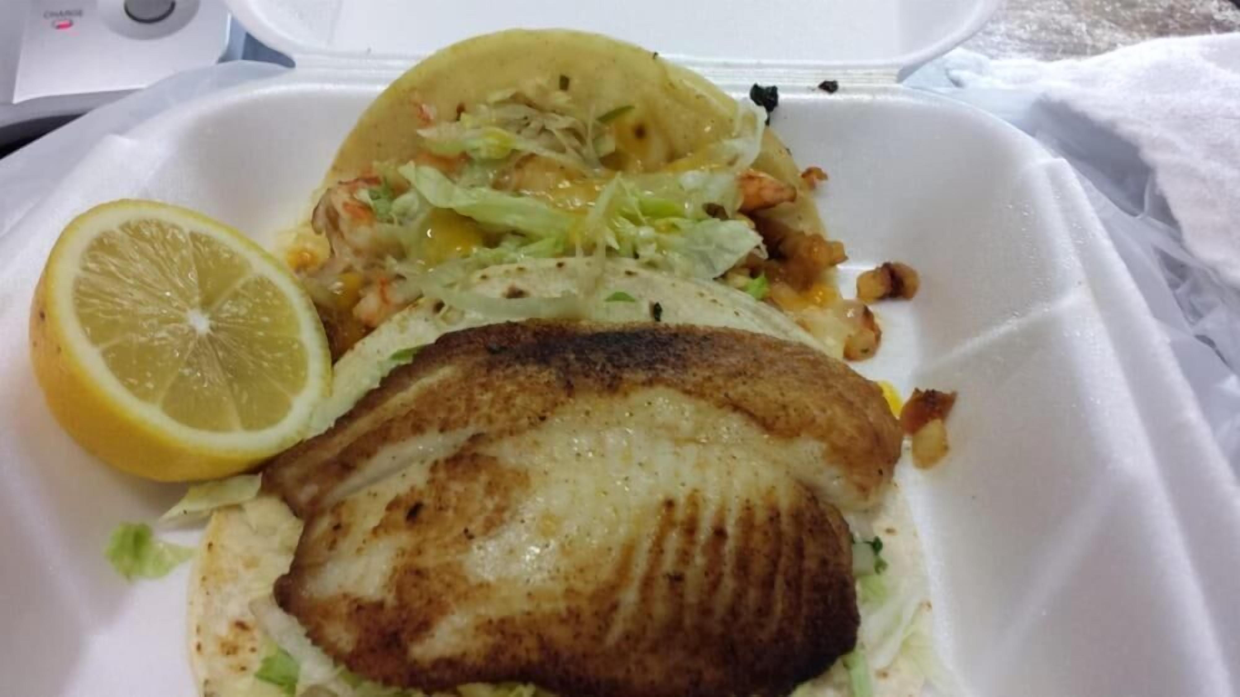 Refeição em embalagem para viagem, com filé de peixe, uma fatia de limão e salada de repolho.
