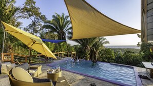 Área da piscina com espreguiçadeiras, deck de madeira e vista para o oceano.