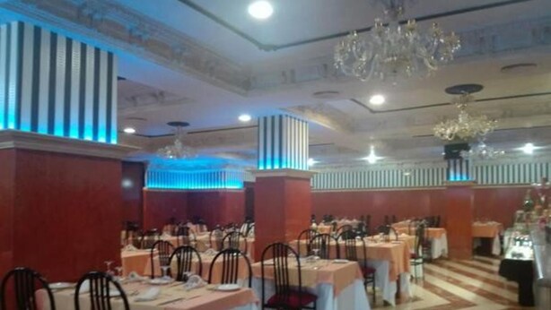 Um restaurante com várias mesas e cadeiras, um candelabro e um chão estampado.