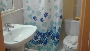 Casa de banho com uma sanita, uma pia branca e uma cortina de chuveiro com motivos florais azuis.