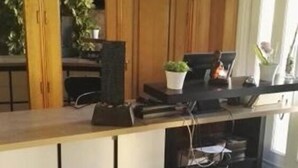 Uma cozinha com armários de madeira, bancada com um laptop e piso revestido de azulejos.