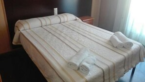 Uma cama bem arrumada com um espelhado listrado e duas toalhas enroladas ao lado.