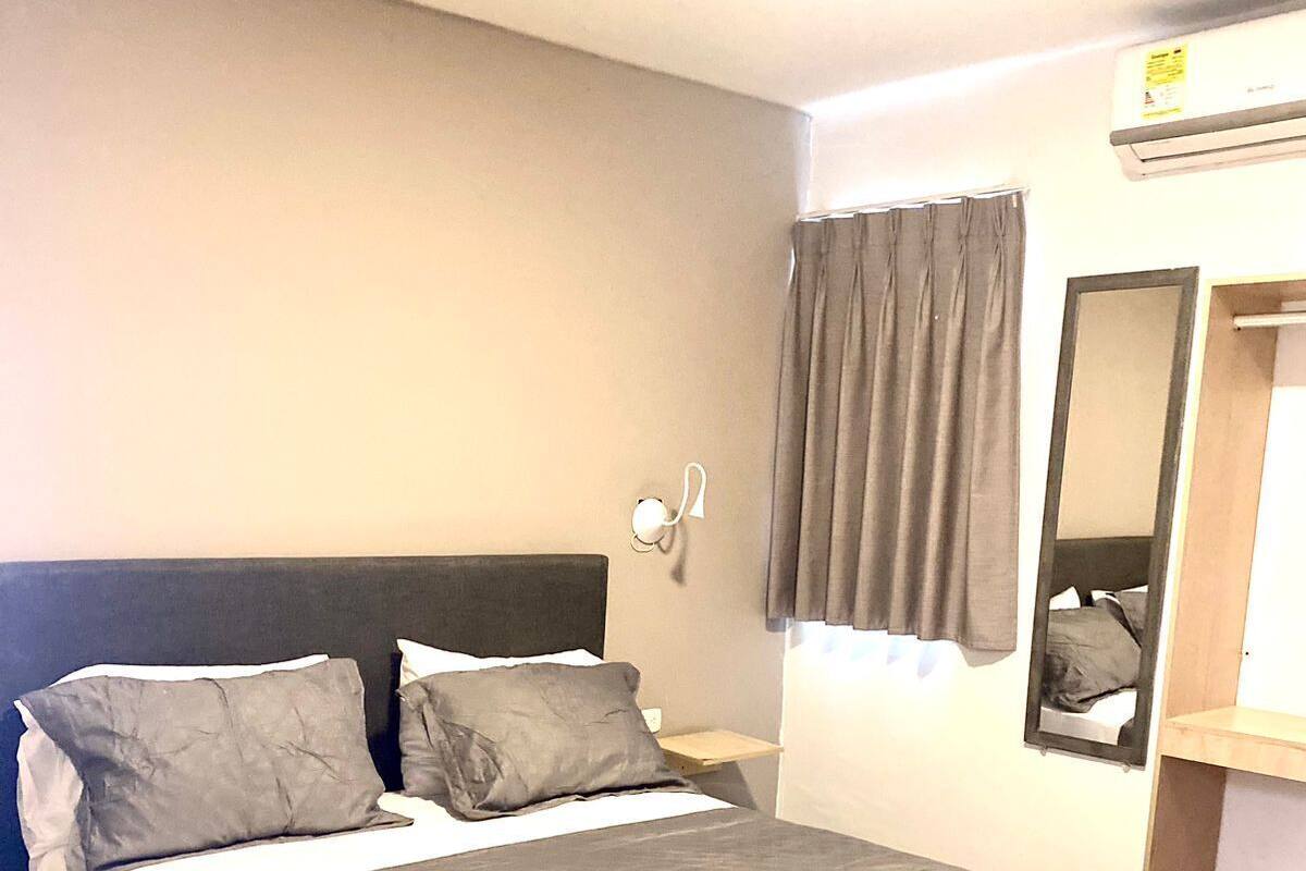 Quarto de hotel com cama, mesa de cabeceira, espelho, ar condicionado fixado na parede e janela com cortinas.