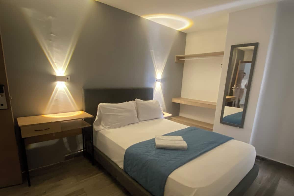 Quarto de hotel com cama, mesa de cabeceira e espelho na parede.