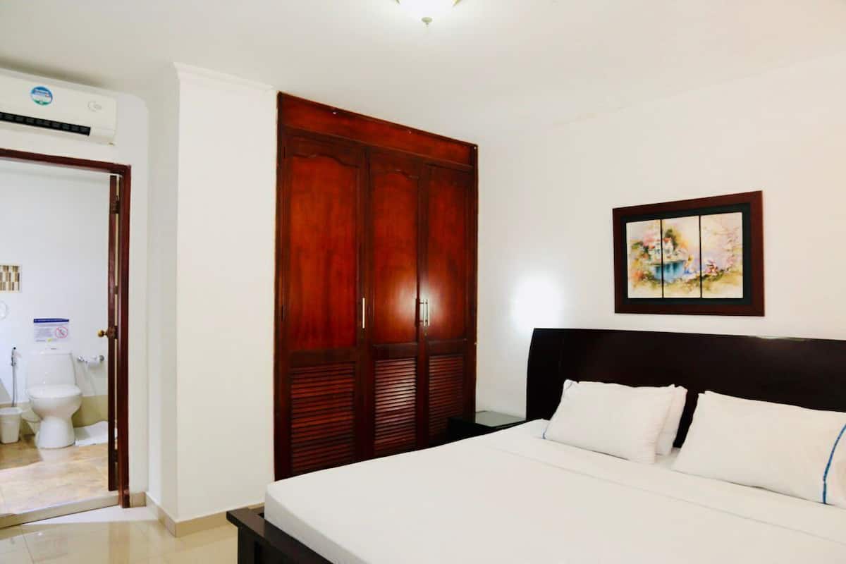 Quarto com cama, guarda-roupa de madeira, quadro na parede e ar condicionado.