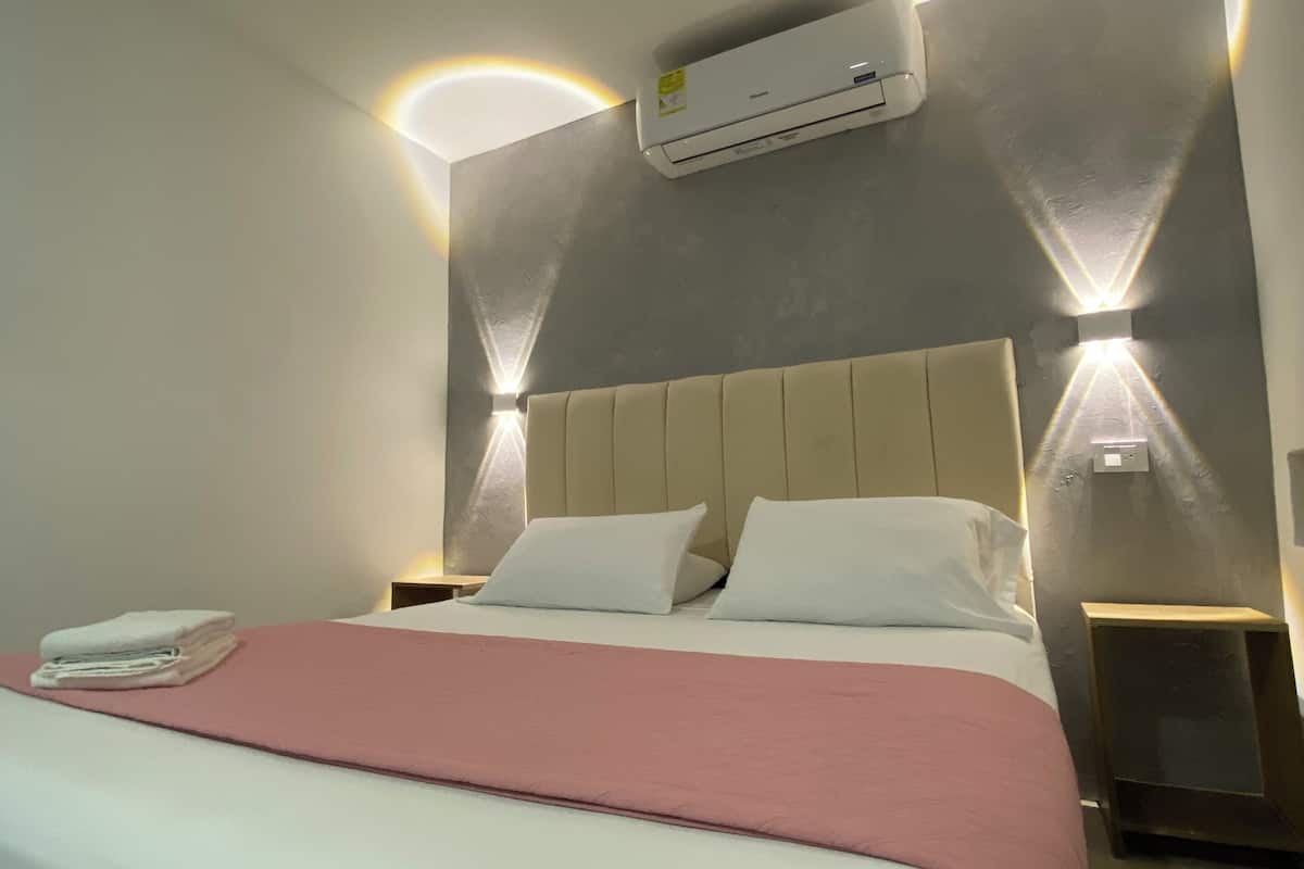Quarto de hotel com uma cama, ar condicionado fixado na parede e duas luminárias de parede.