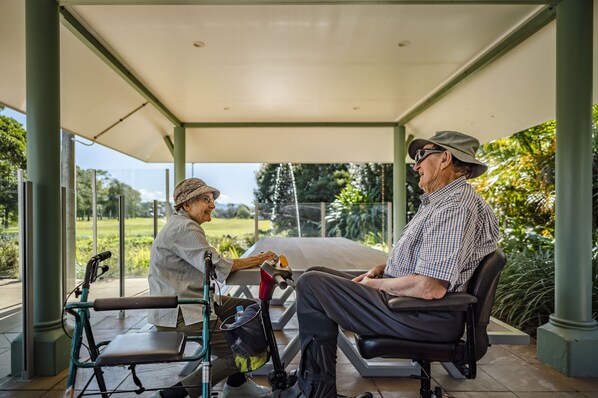 Uma área de estar coberta ao ar livre, com um banco e uma cadeira de rodas.