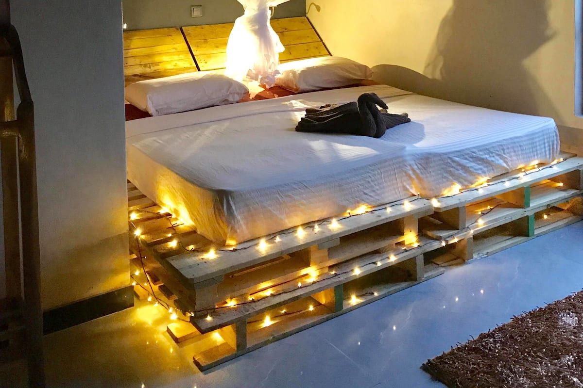Uma cama com dossel, estrado de madeira sob o colchão e luzes de fada.