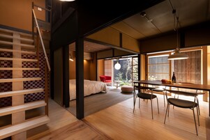 Interior moderno com escada de madeira, área de jantar com mesa e cadeiras, e uma cama ao fundo.