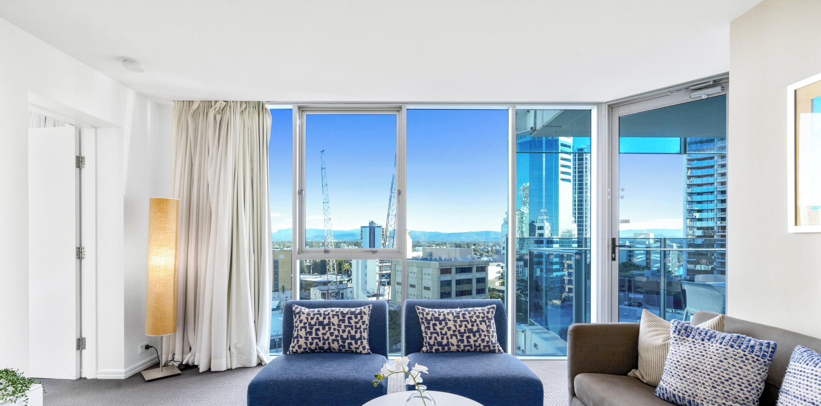Uma sala de estar moderna com um conjunto de sofás, uma mesa de centro e vista para o horizonte urbano através de grandes janelas.