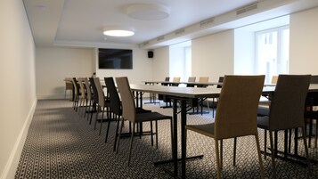 Sala de conferências com uma mesa comprida e cadeiras, piso coberto por carpete e grandes janelas.