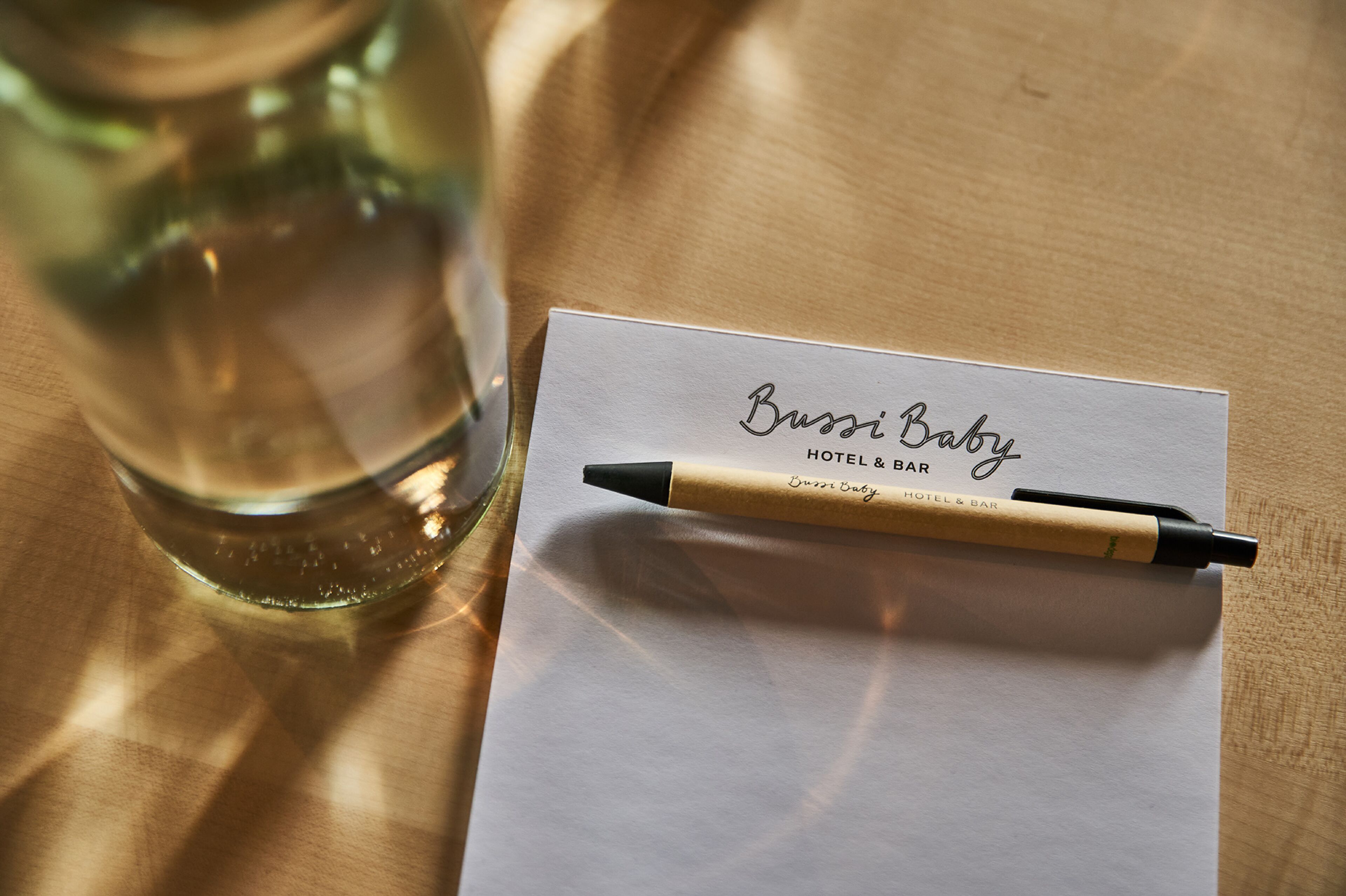 Um copo de água, uma caneta e um pedaço de papel com a inscrição "Bussi Baby HOTEL & BAR".