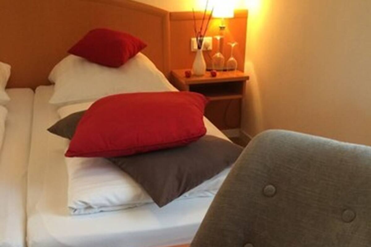 Quarto de hotel com cama, almofadas, mesa de cabeceira com luminária e cadeira com toalha e pimentas vermelhas.