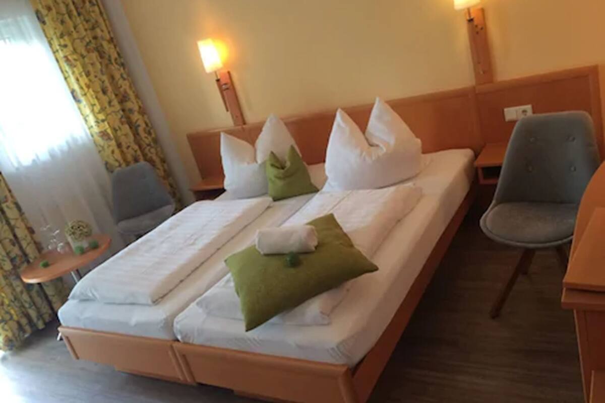 Quarto de hotel com cama, duas cadeiras, mesa de cabeceira e abajur.