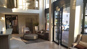 Um lobby espaçoso com design moderno, apresentando uma área de estar com sofás e poltronas, uma mesa de centro e um balcão de recepção.
