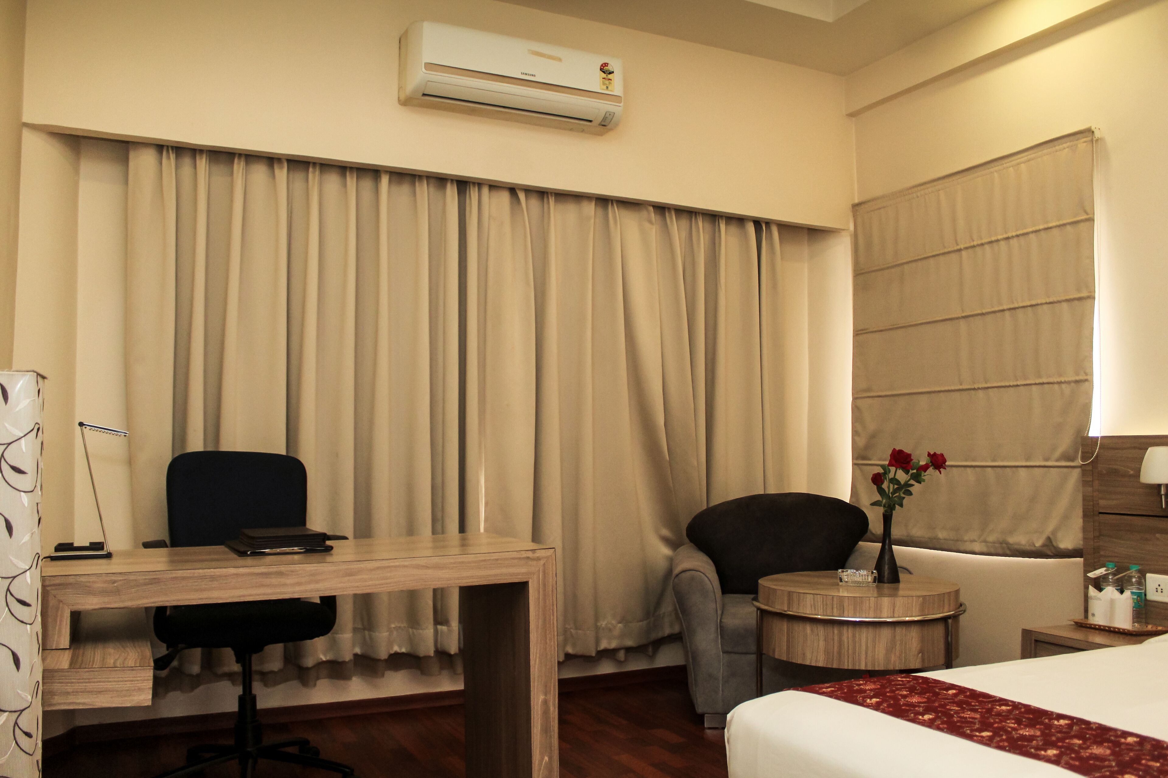 Quarto de hotel com uma escrivaninha, uma cadeira, uma mesa redonda pequena, uma cama, uma mesinha de cabeceira e um ar condicionado fixado na parede.