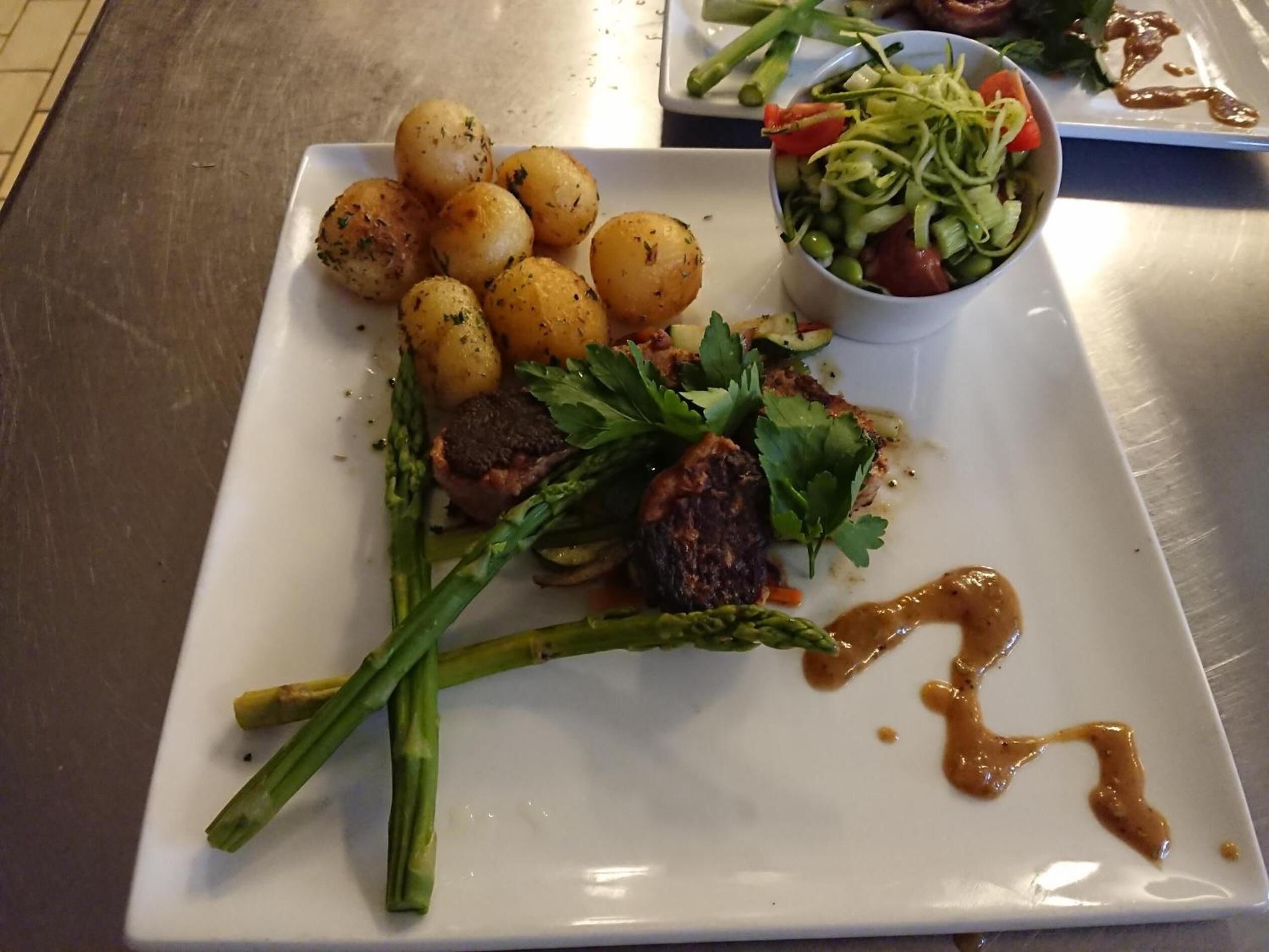Prato com batatas assadas, aspargos e um prato de carne, acompanhado de uma salada e molho.