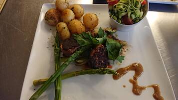 Prato com batatas assadas, aspargos e um prato de carne, acompanhado de uma salada e molho.