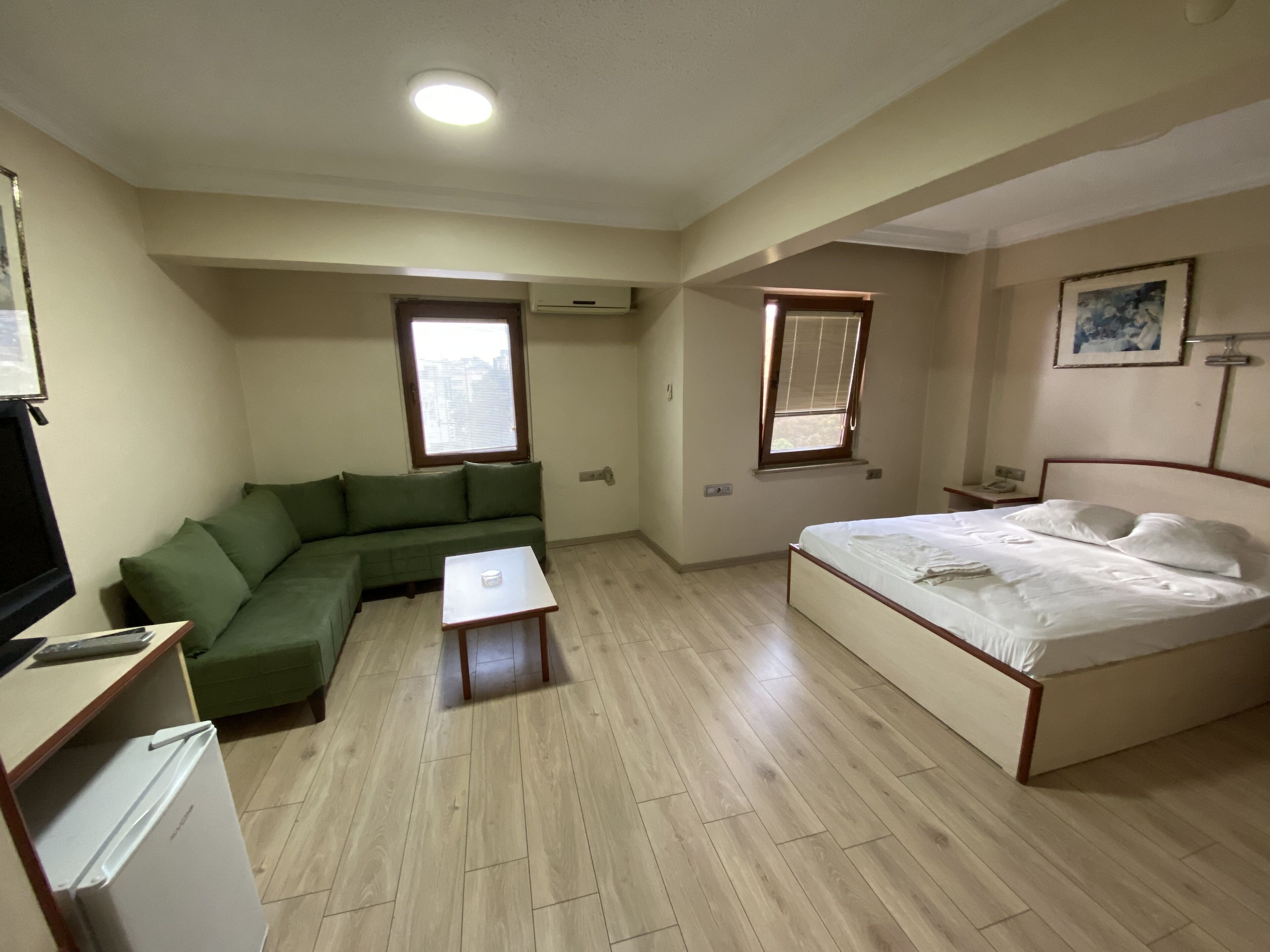 Um quarto com uma cama, um sofá verde, uma mesinha e uma geladeira.