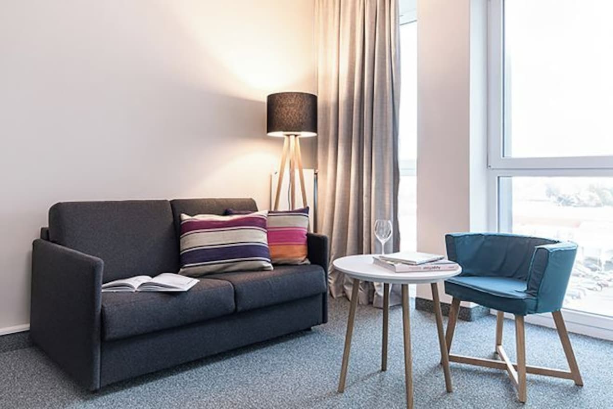 Quarto moderno com sofá, mesa redonda pequena, cadeira e abajur.