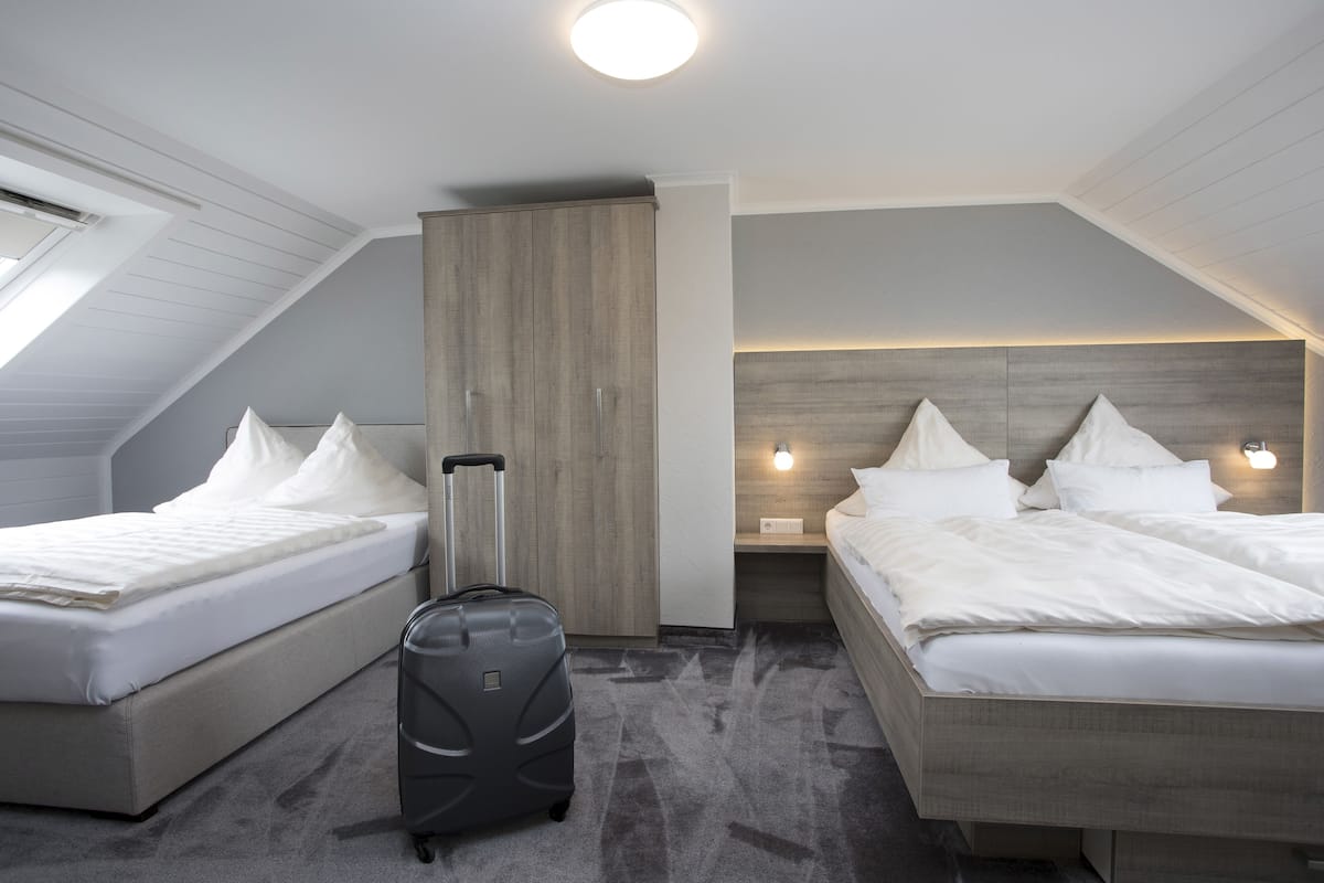 Quarto de hotel com duas camas, um guarda-roupa, uma mala e um claraboia.