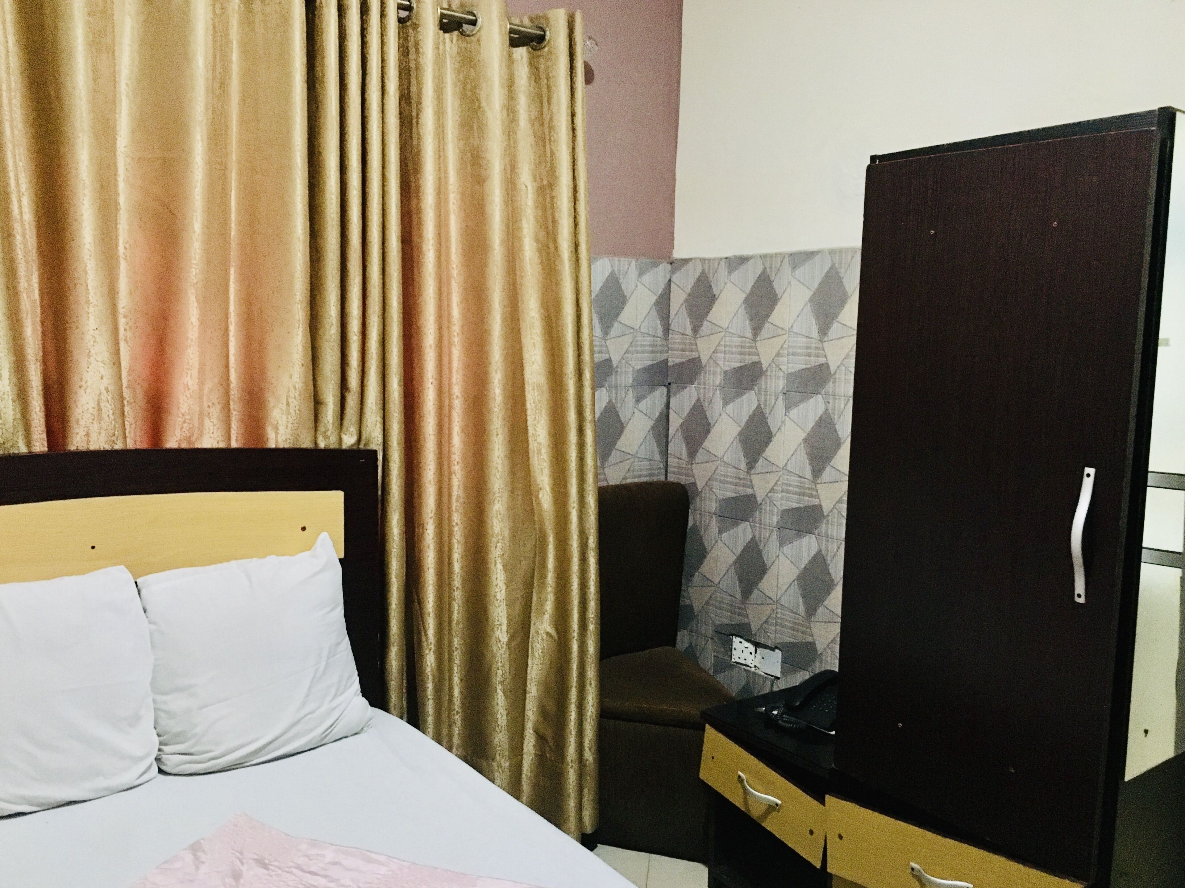 Quarto de hotel com cama, escrivaninha, guarda-roupa e parede estampada.