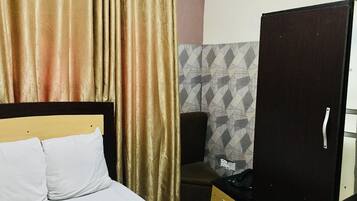 Quarto de hotel com cama, escrivaninha, guarda-roupa e parede estampada.