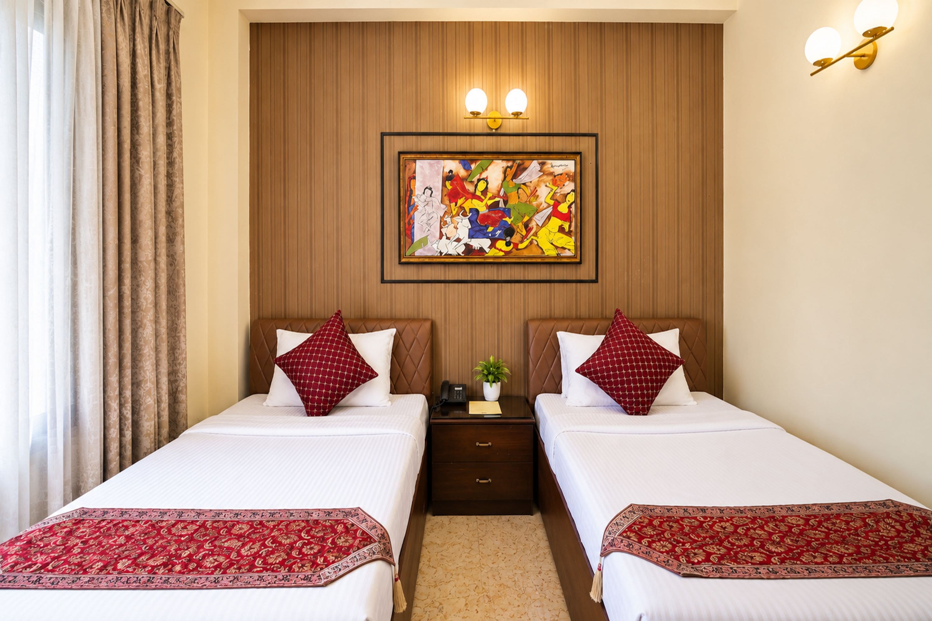 Quarto de hotel com duas camas, cabeceira com pintura, mesas de cabeceira, telefone e uma pequena planta.