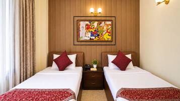 Quarto de hotel com duas camas, cabeceira com pintura, mesas de cabeceira, telefone e uma pequena planta.
