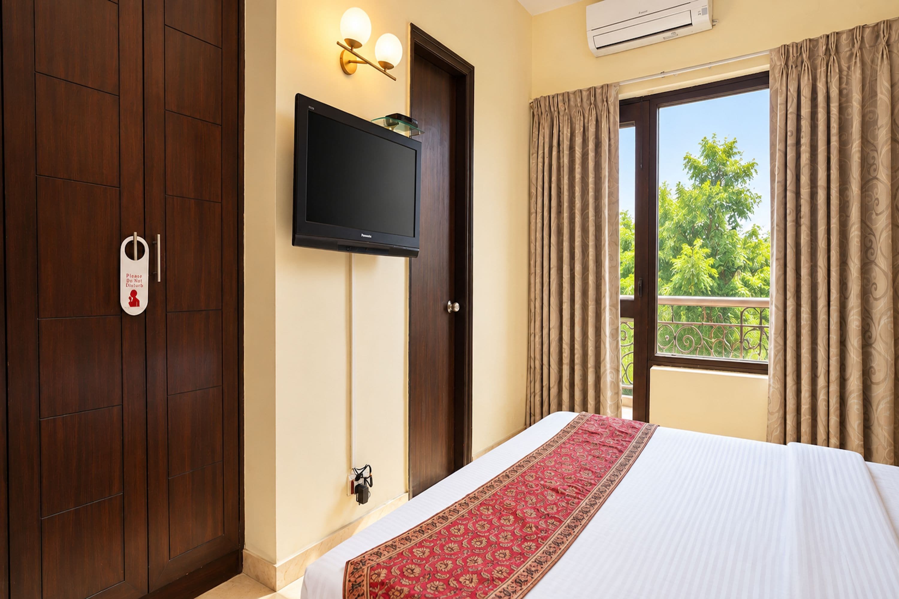Quarto de hotel com cama, televisão na parede, guarda-roupa e janela com cortinas.