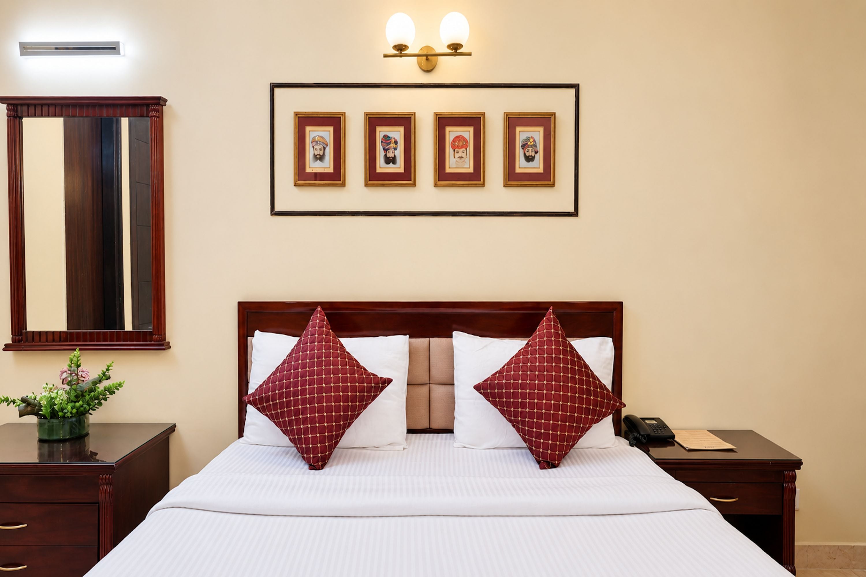 Quarto de hotel com uma cama grande, duas mesas de cabeceira, um criado-mudo, uma luminária na parede e uma obra de arte emoldurada sobre a cama.
