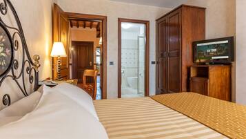 Quarto de hotel com cama, televisão, móveis de madeira e banheiro visível através de uma porta aberta.