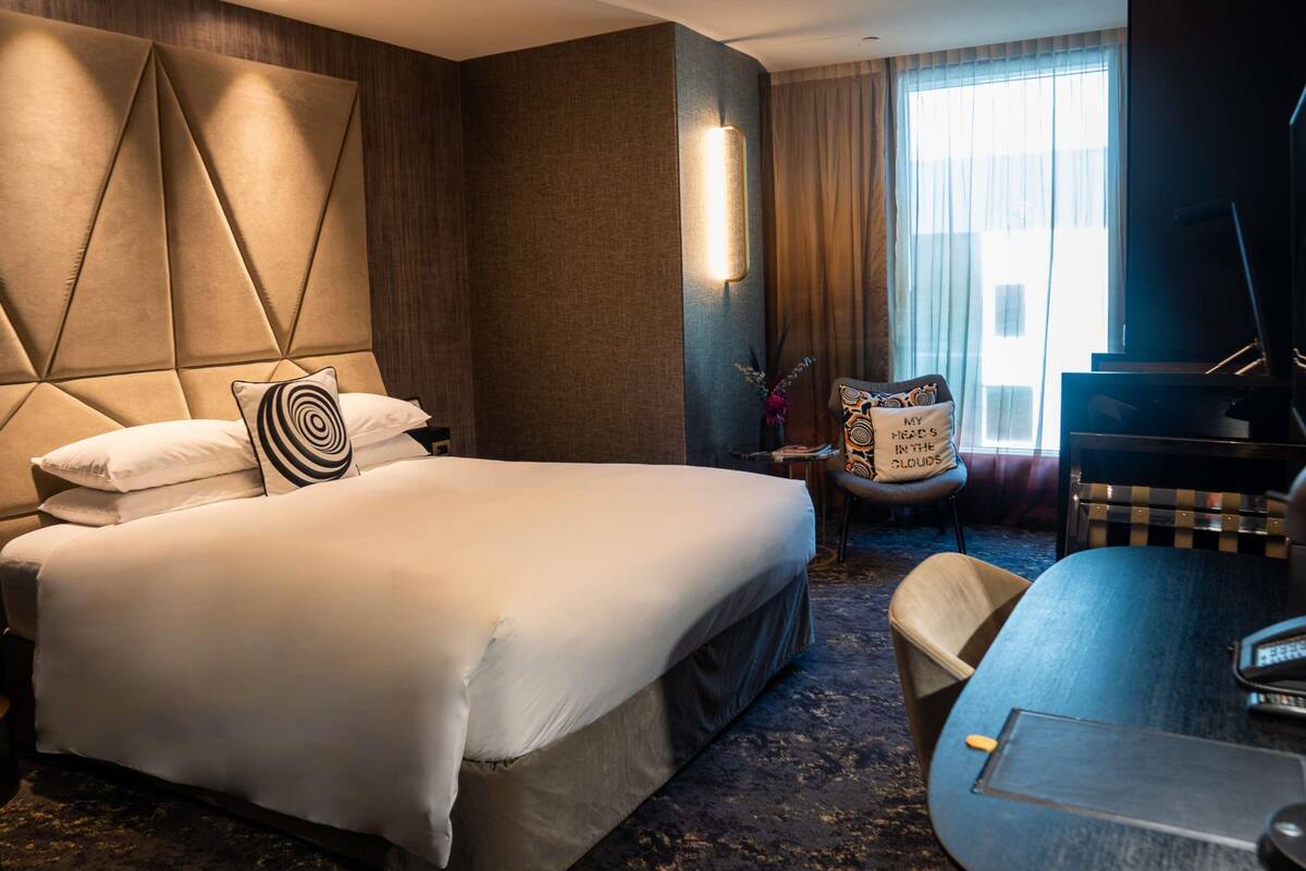 Quarto de hotel com cama grande, escrivaninha, cadeira, piano e janela com cortinas.
