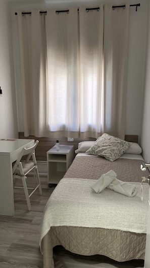 Quarto com cama, escrivaninha, cadeira, mesa de cabeceira e janela com cortinas.