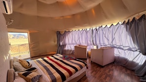 Um quarto tipo tenda espaçoso, com uma cama grande, duas cadeiras e vista para o deserto pelas cortinas.