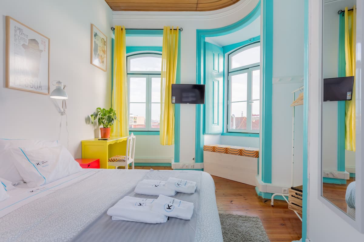 Quarto de hotel moderno com uma cama grande, uma televisão e vista para a cidade.