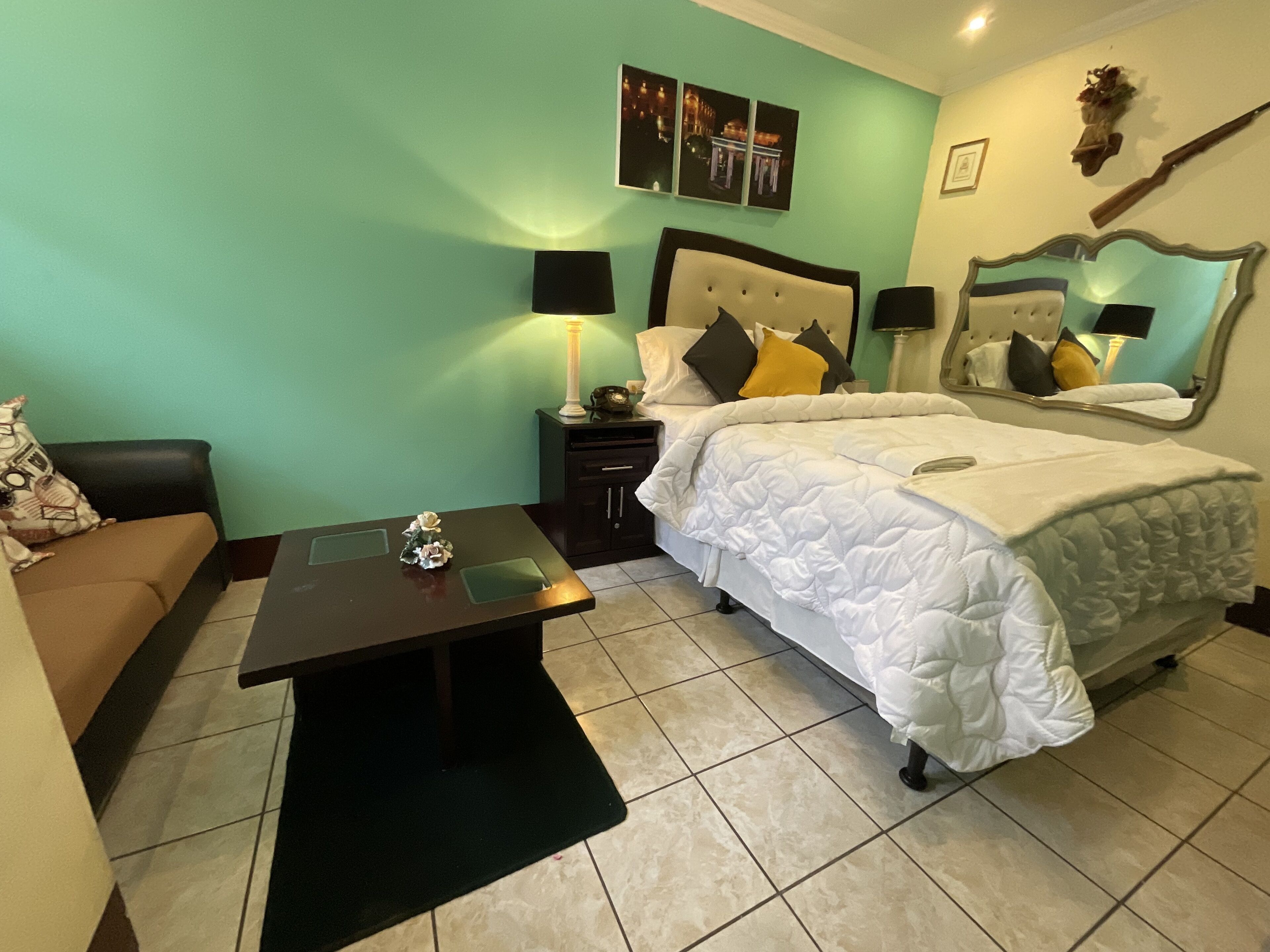Quarto de hotel com cama, mesa de cabeceira, mesa, cadeira e espelho.
